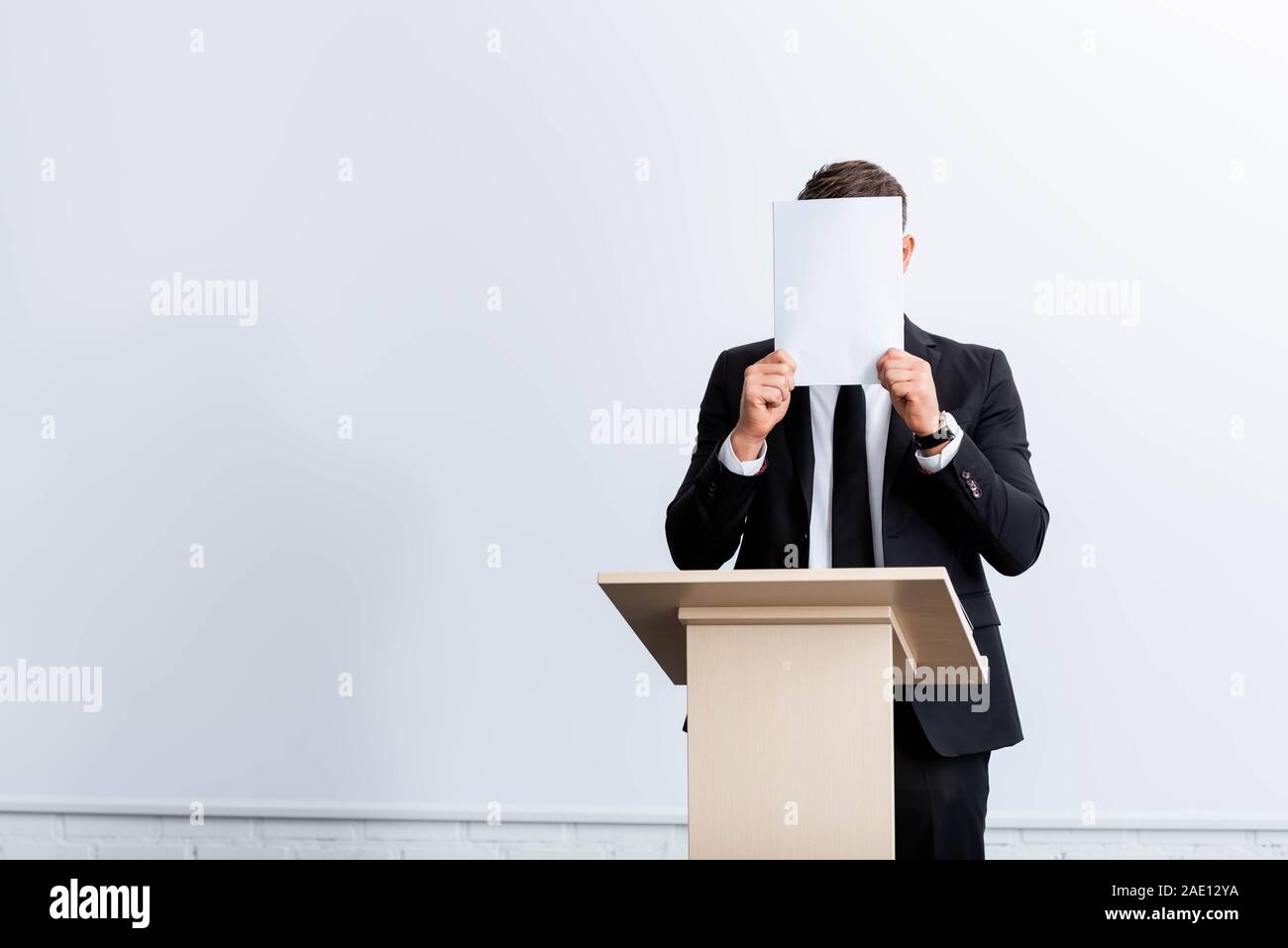 scared businessman in suit standing at podium tribune and obscuring ...