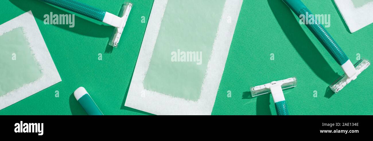 top view of green disposable razors and depilation wax stripes on green ...