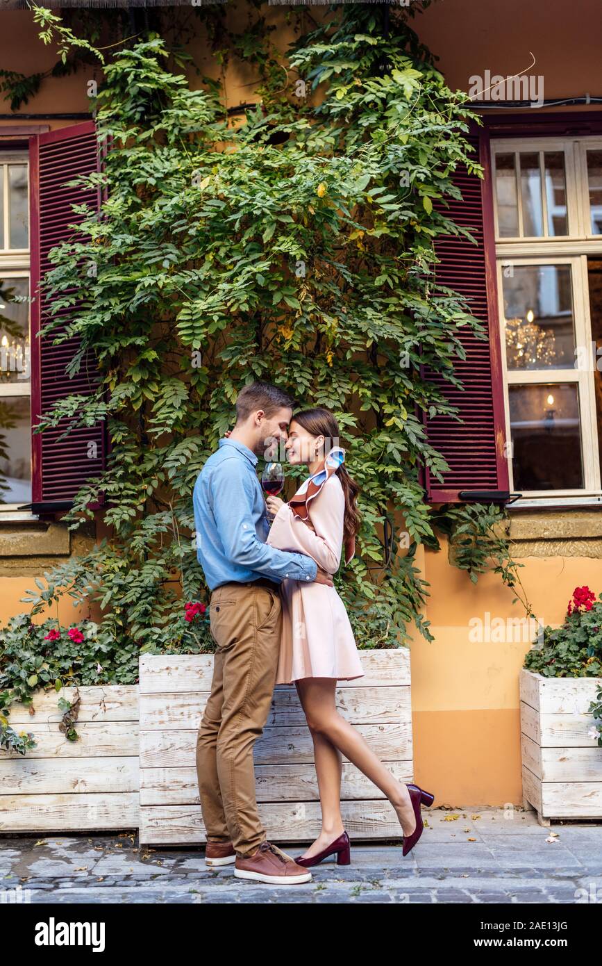 side view of happy young couple embracing while standing near house ...