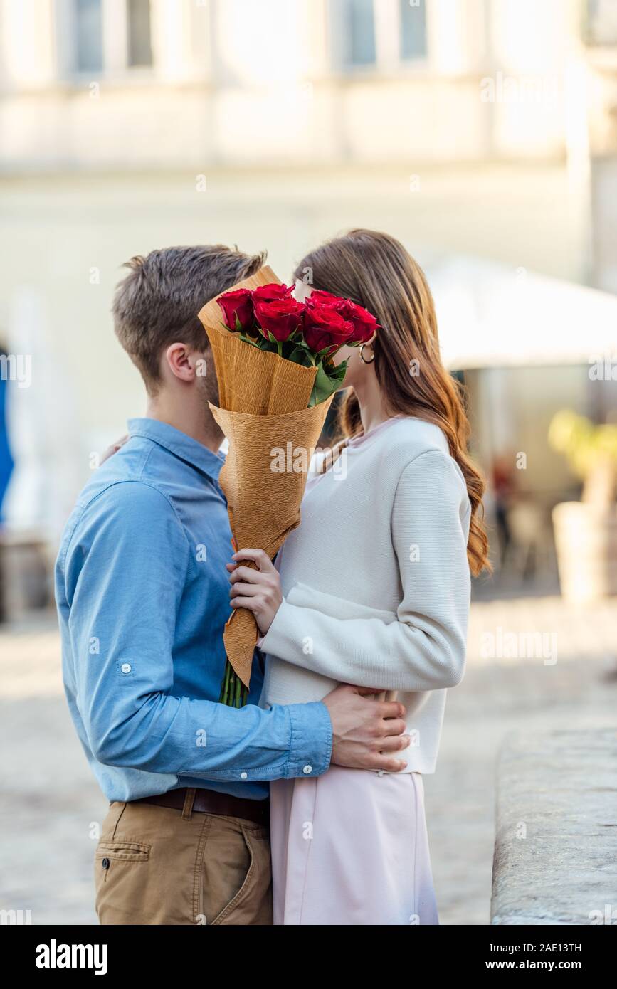 happy couple kissing while hiding behind bouquet of red roses Stock ...
