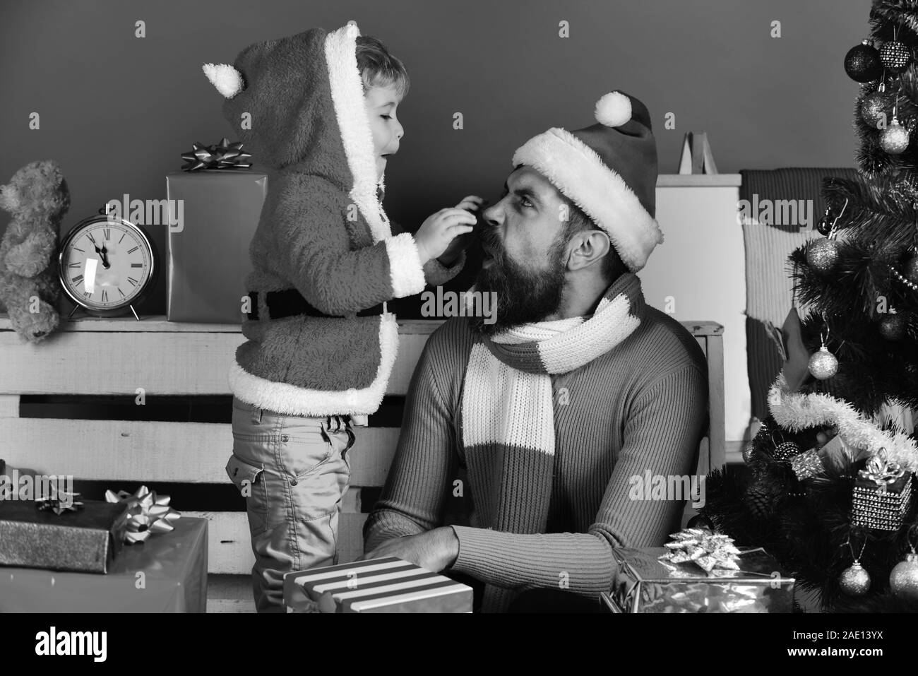 Santa and little assistant among gift boxes by fir tree. Man with beard ...