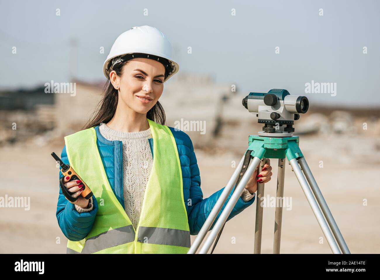 Attractive surveyor with digital level and radio set smiling at camera ...