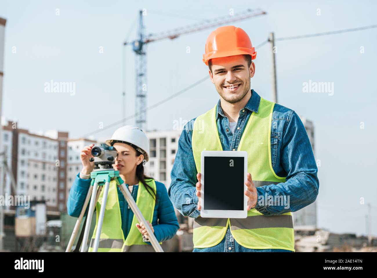Smiling surveyor holding digital tablet with blank screen and colleague ...
