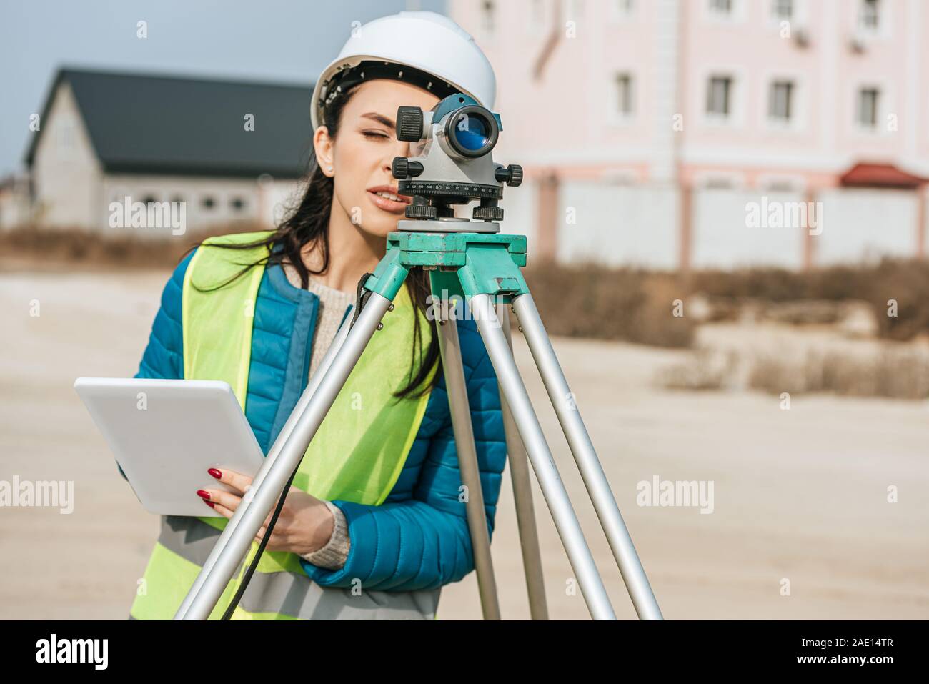 Female surveyor with digital tablet looking through measuring level ...