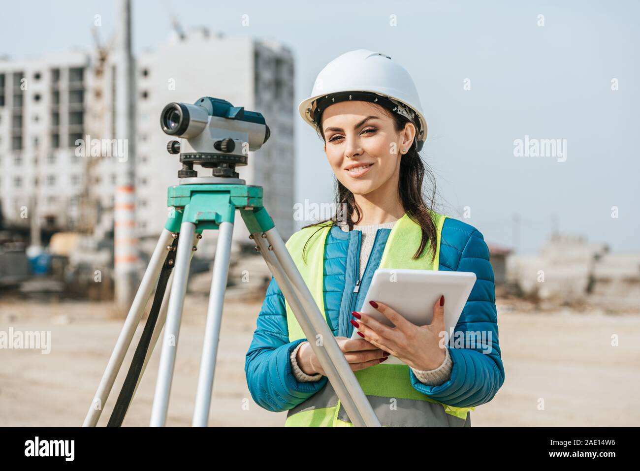 Surveyor with digital tablet and measuring level smiling at camera ...