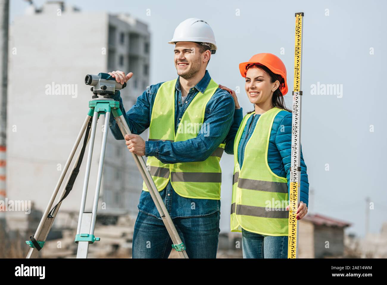 Smiling surveyors with ruler and digital level looking away Stock Photo ...