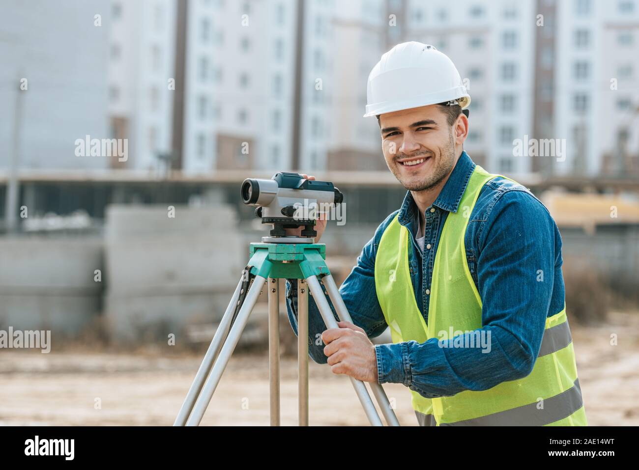 Smiling surveyor with digital level looking at camera on construction ...