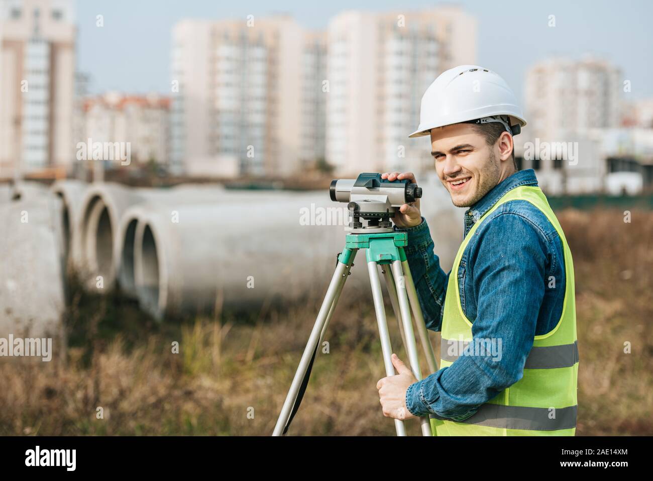 Surveyor with digital level smiling at camera with building materials ...