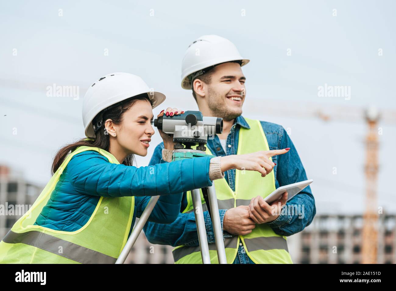 Surveyor looking through digital level and pointing away to colleague ...