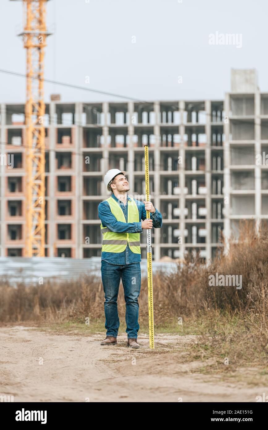 Smiling surveyor holding ruler with construction site at background ...