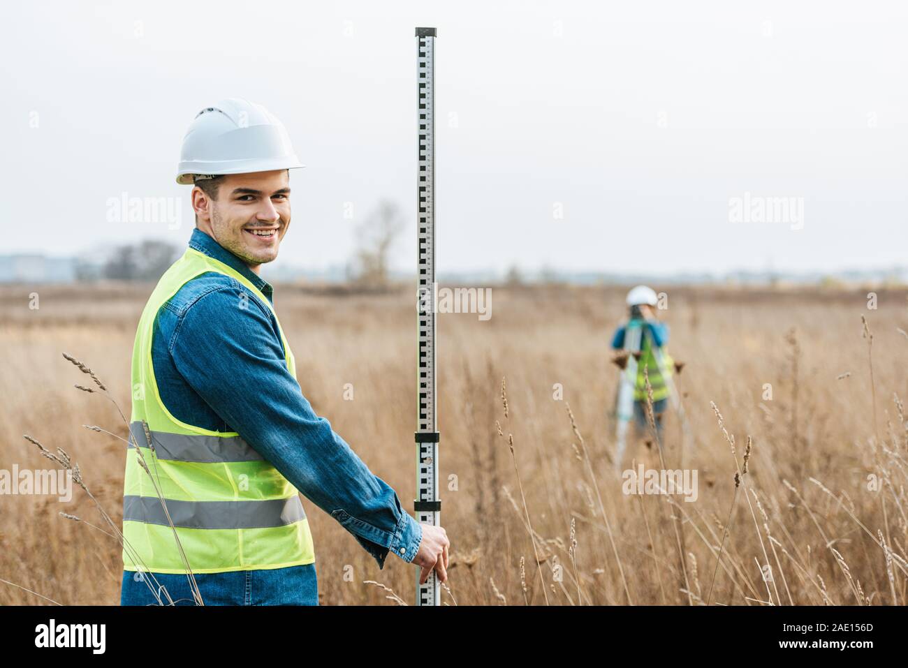 Selective focus of smiling surveyor with ruler and colleague with ...