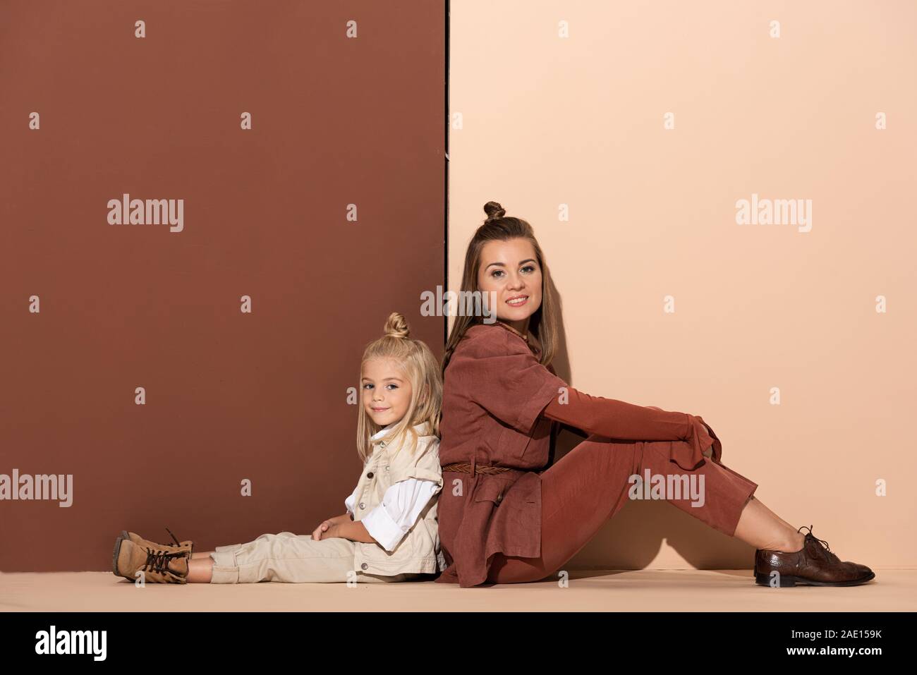 smiling daughter and mother looking at camera on beige and brown ...