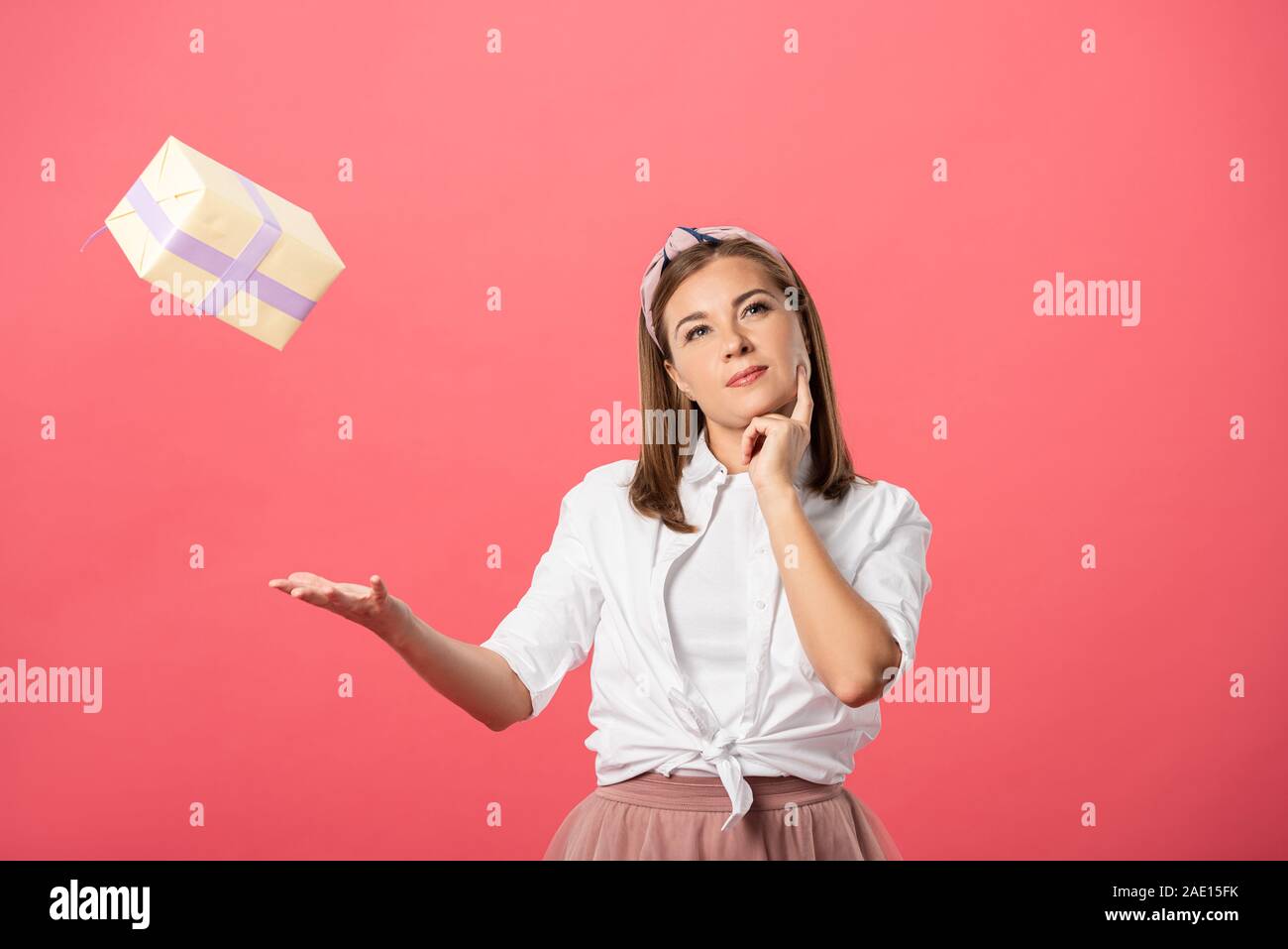 attractive and pensive woman throwing gift box isolated on pink Stock ...