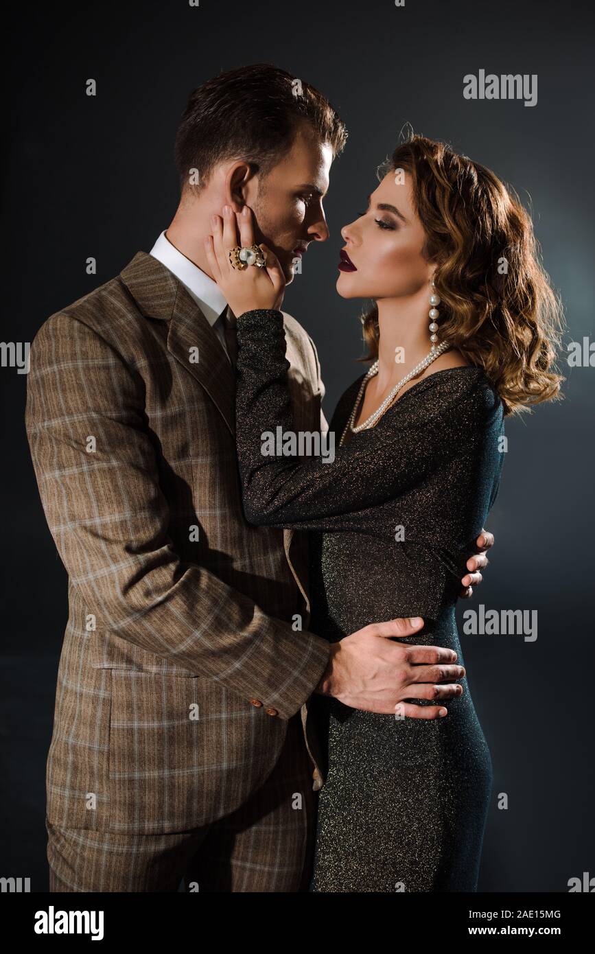 side view of attractive woman looking at handsome gangster on black ...