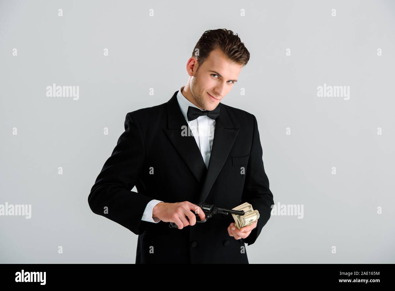 happy criminal man holding gun and dollar banknotes isolated on grey ...