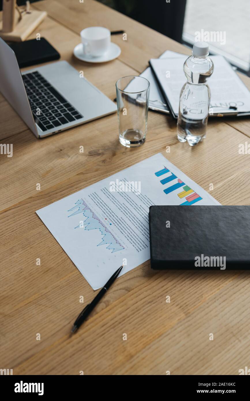 wooden table with notebook, paper with infographics, bottle of water ...