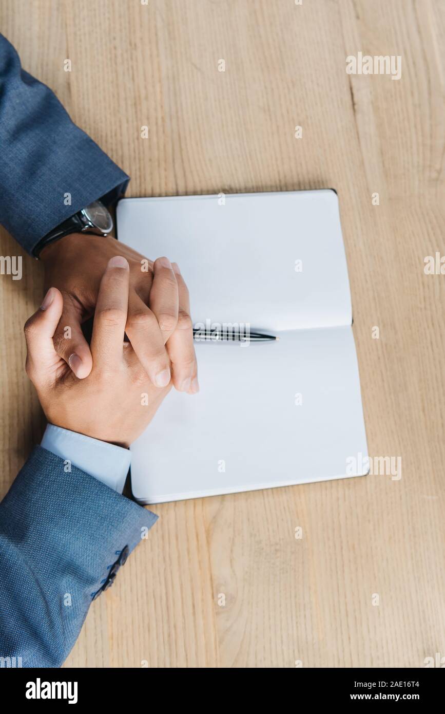 cropped view of businessman sitting with clenched hands near blank ...