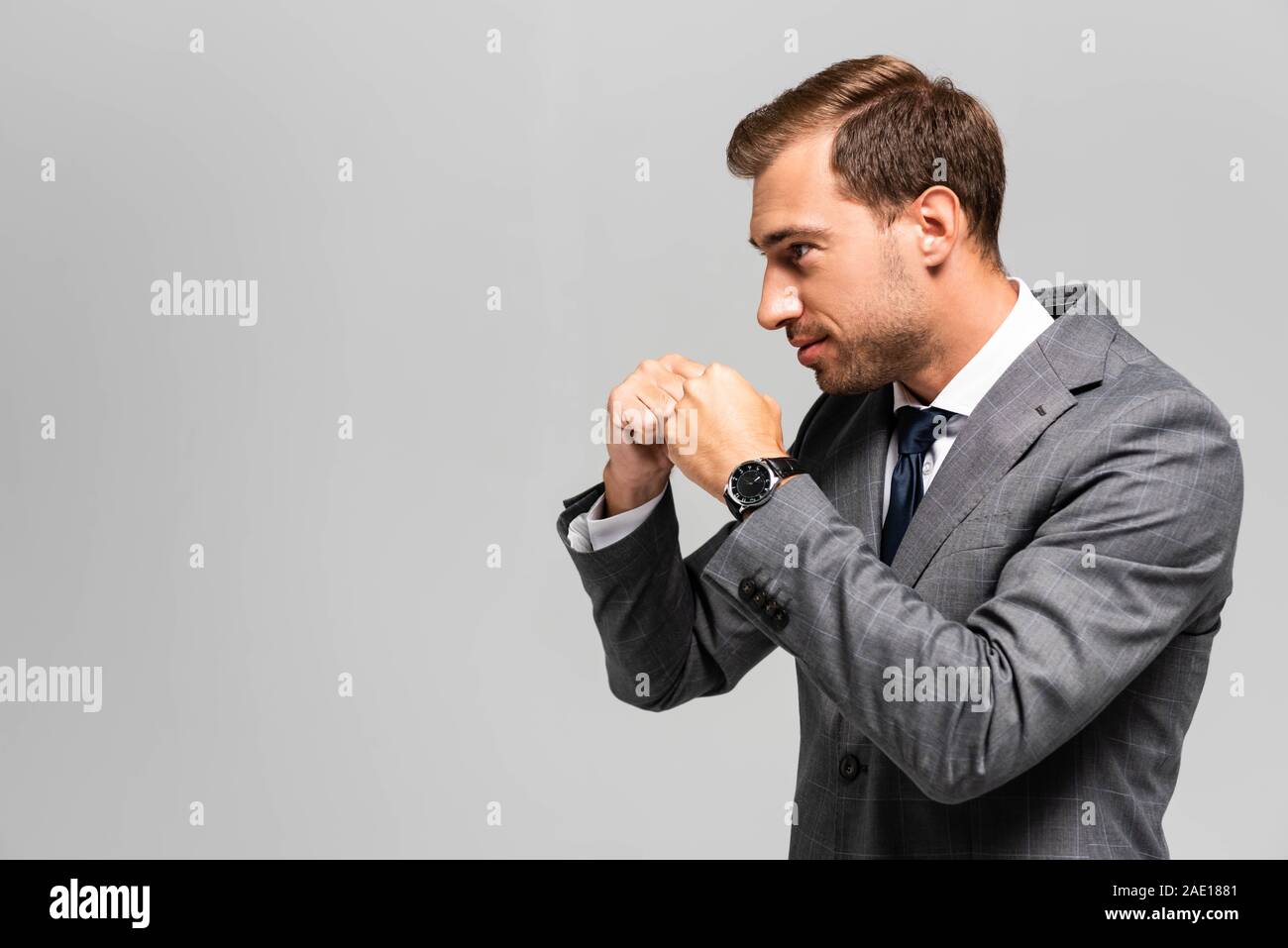 side view of handsome businessman in suit punching isolated on grey ...