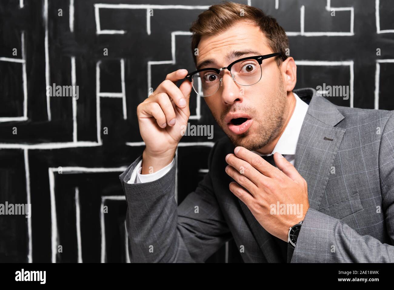 handsome and shocked businessman in suit looking at camera near ...