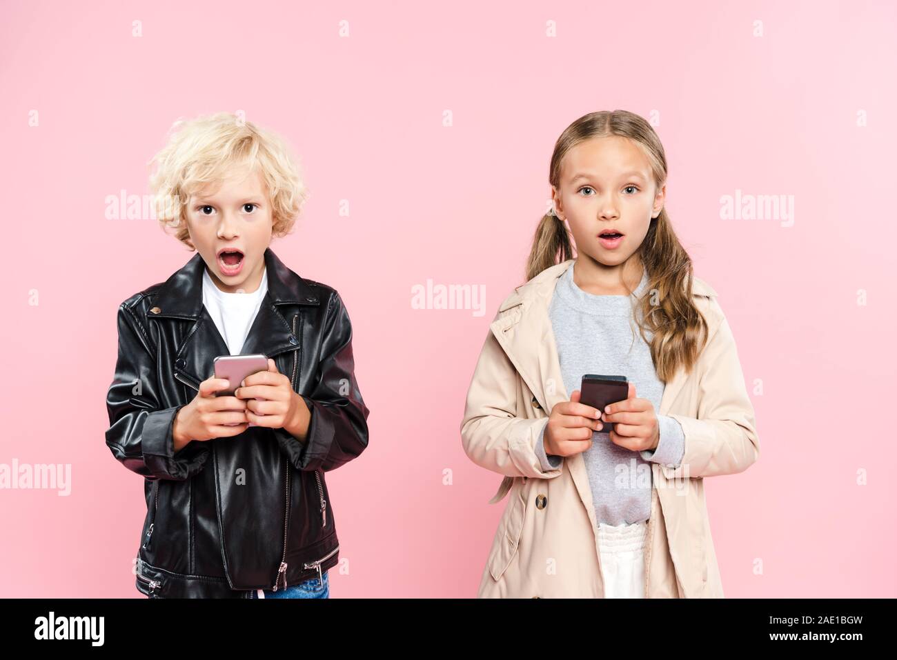 shocked kids holding smartphones and looking at camera on pink ...