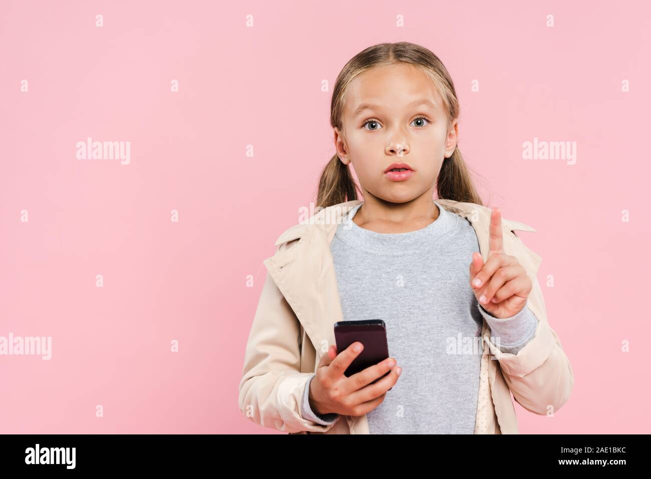 shocked kid showing idea sign and holding smartphone isolated on pink ...