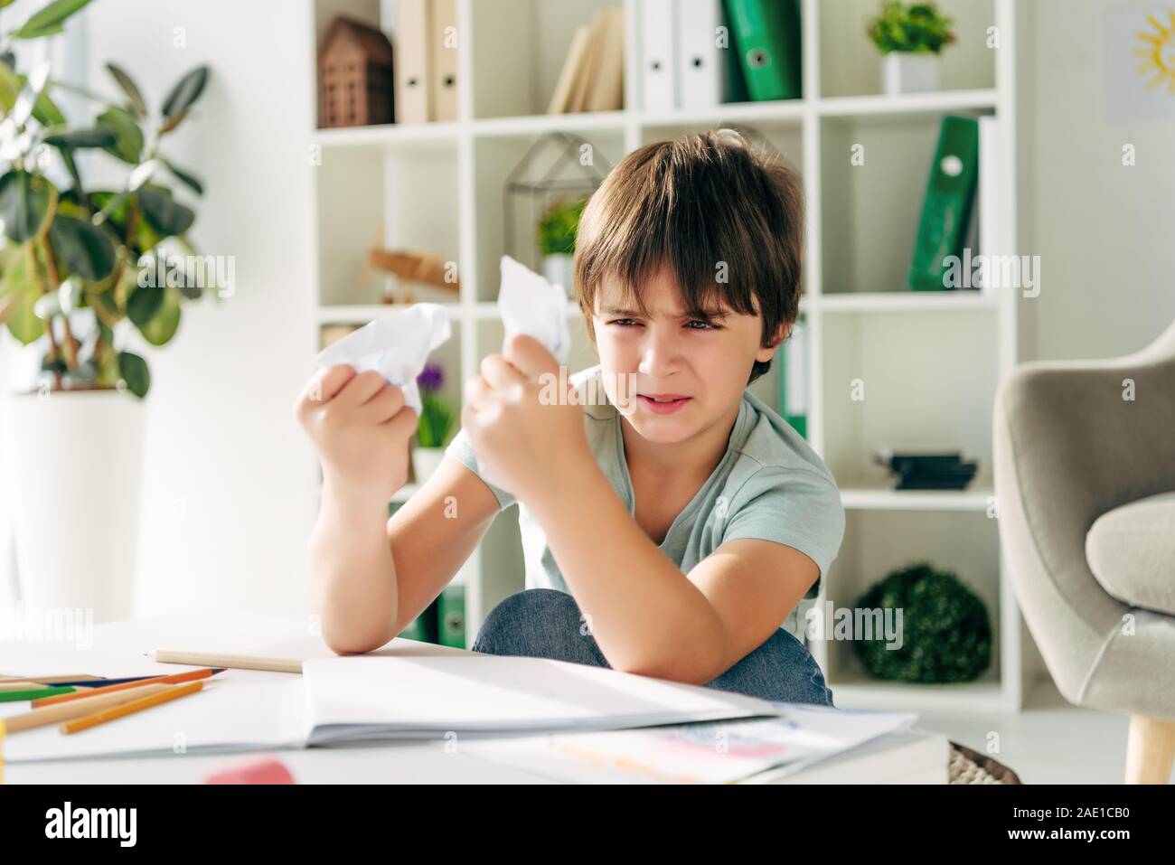 irritated kid with dyslexia holding crumpled papers and sitting at ...