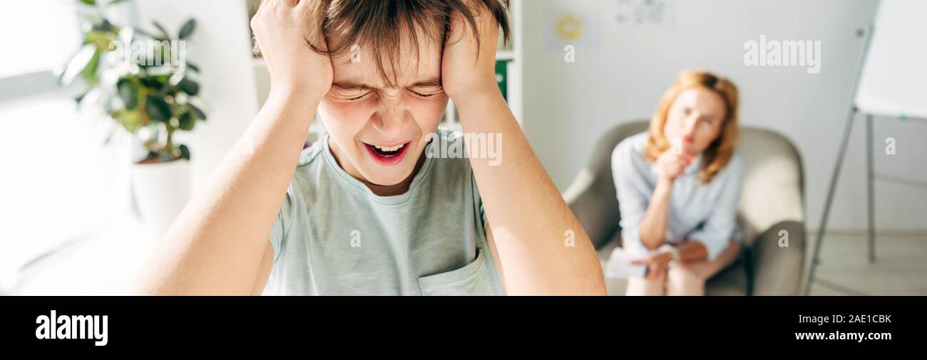 panoramic shot of irritated kid with dyslexia shouting and holding head ...