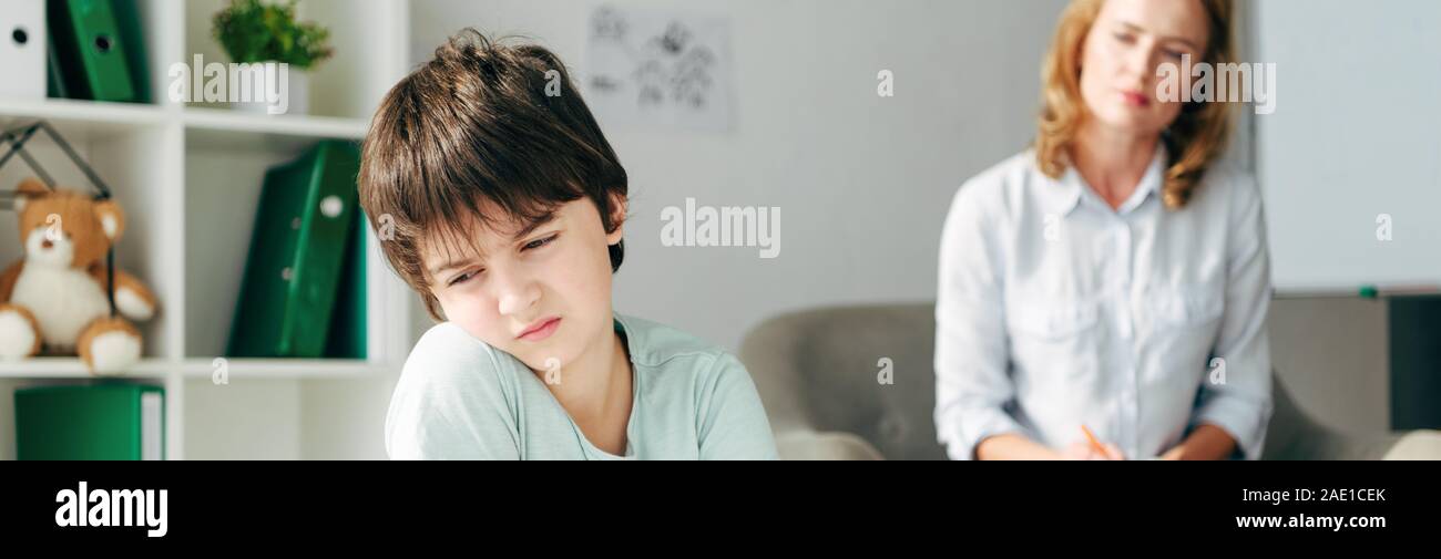 panoramic shot of sad kid with dyslexia and child psychologist looking ...