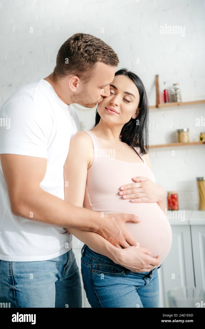 tender husband touching belly of pregnant wife and kissing her in ...