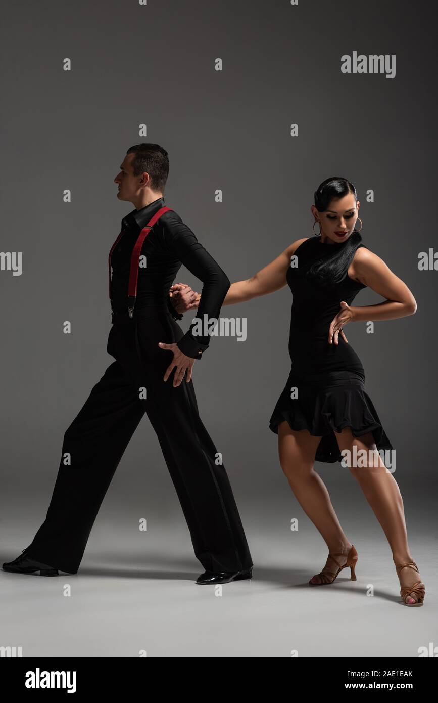 stylish couple of dancers in black clothing performing tango on grey ...