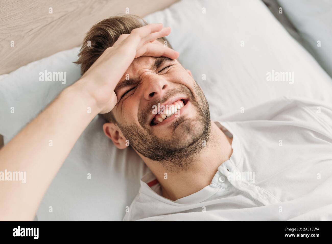 overhead view of young man touching head while suffering from migraine ...