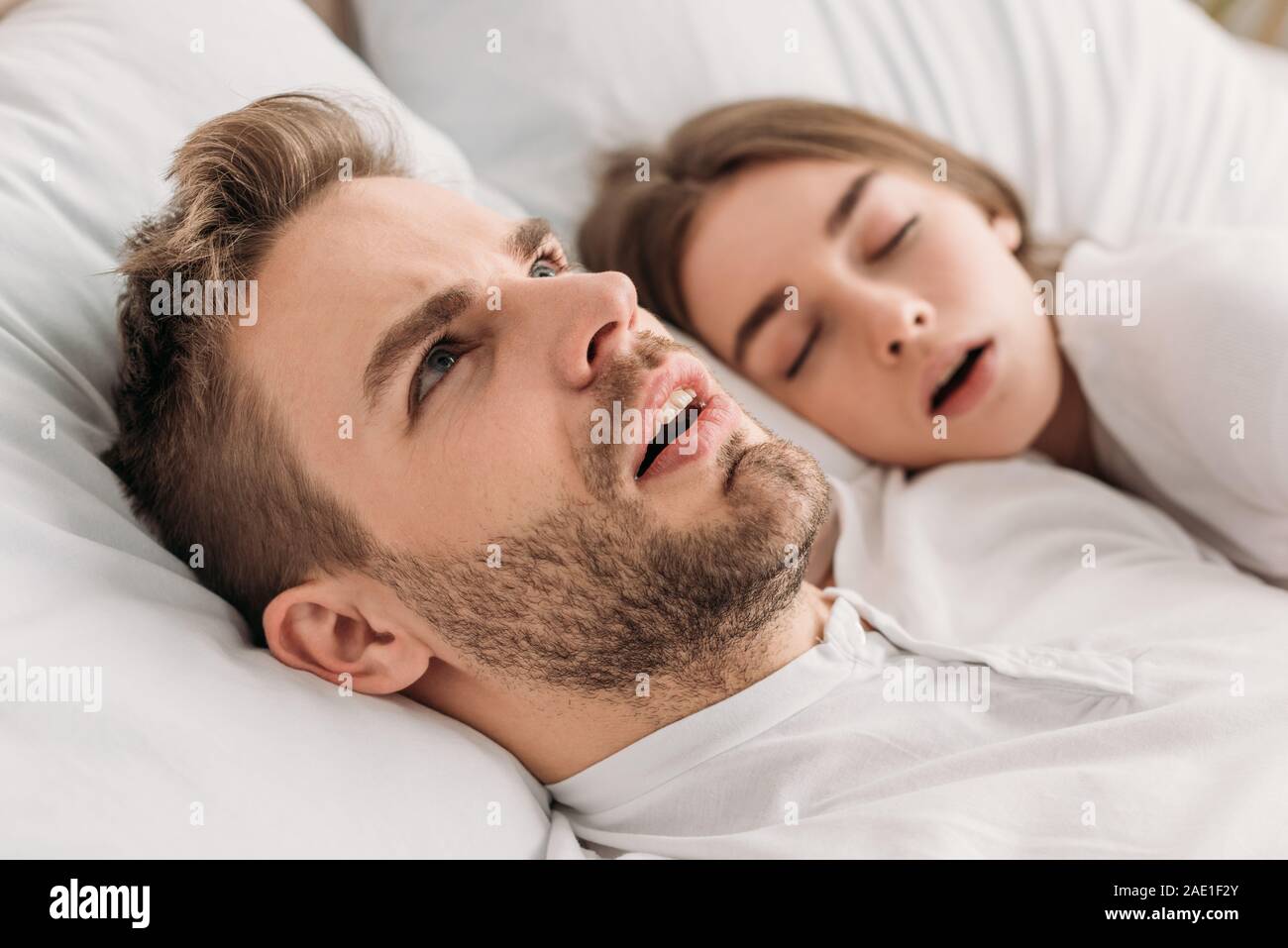 awakened man looking up while lying in bed near snoring wife Stock ...