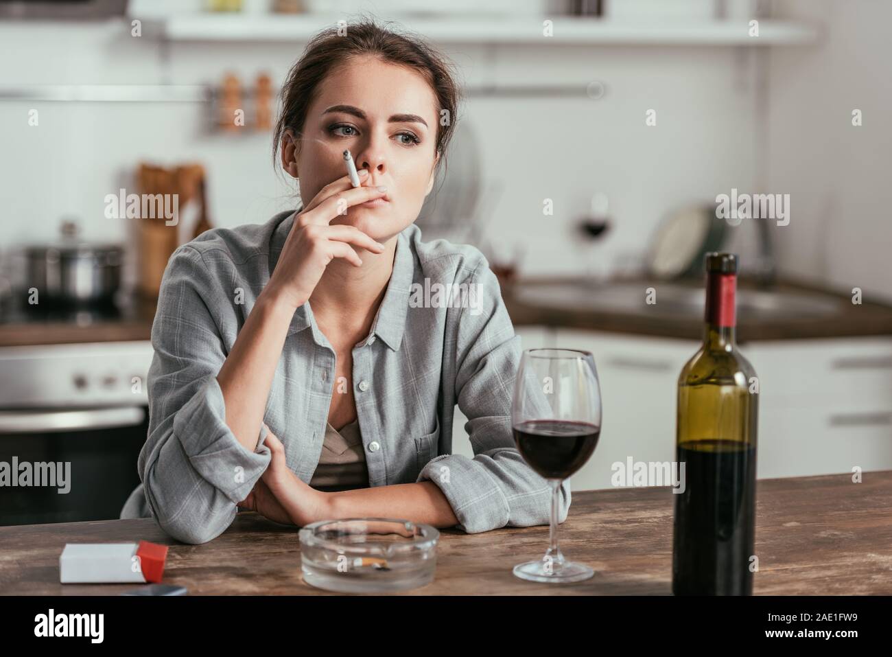 Pensive woman smoking beside wine on kitchen table Stock Photo - Alamy