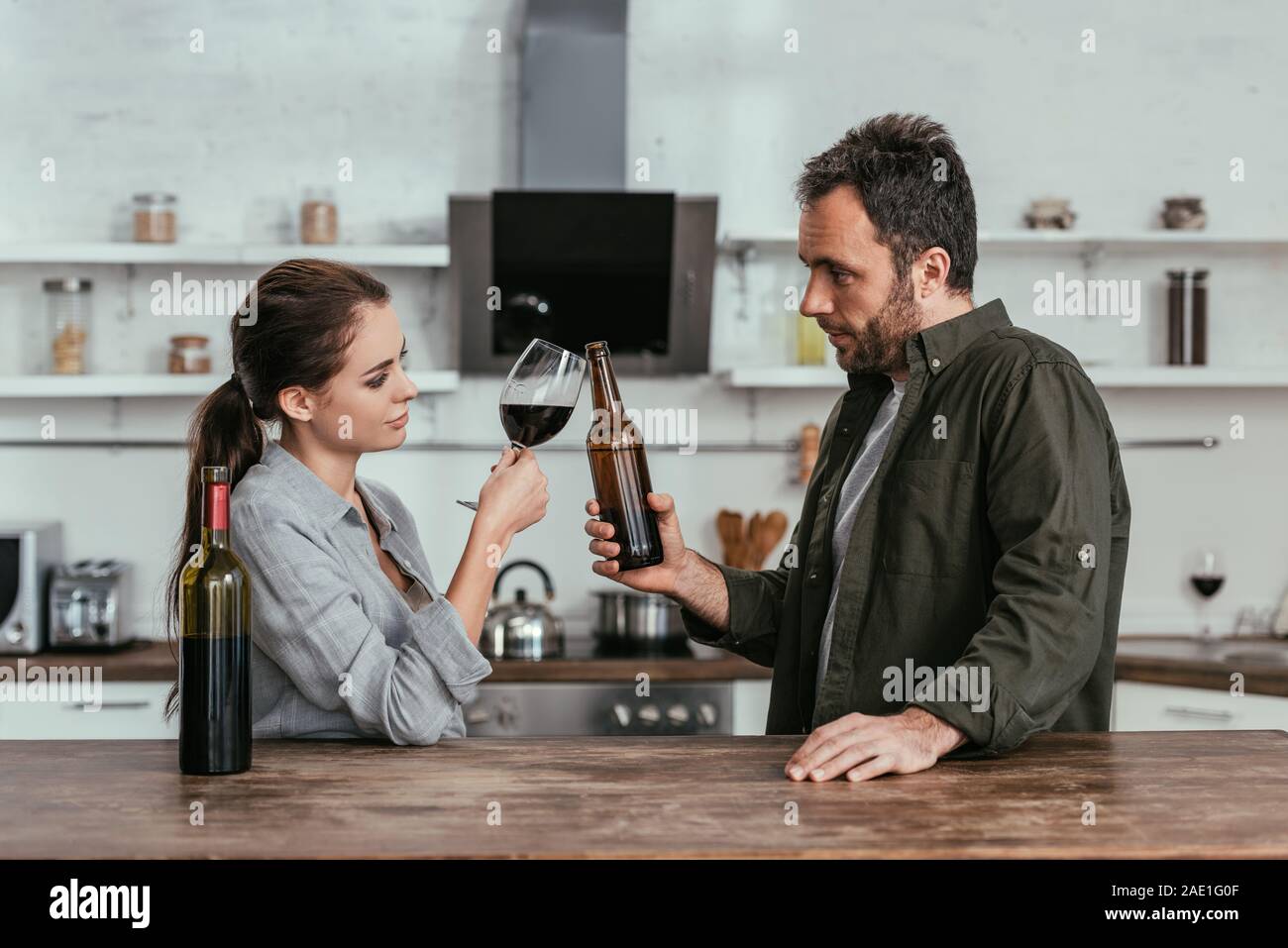Couple with wine and beer clinking at kitchen Stock Photo - Alamy