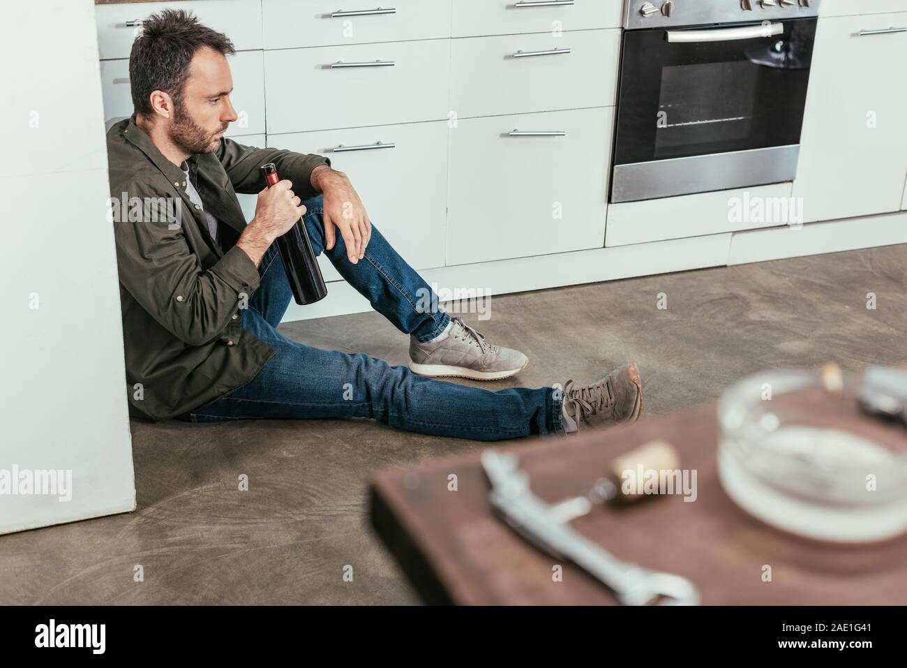 Selective focus of sad man with wine bottle sitting on kitchen floor ...