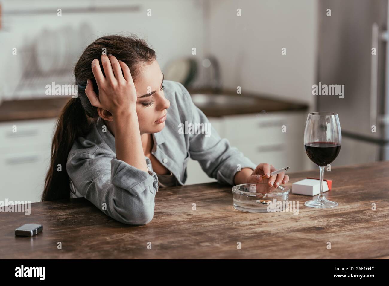 Worried woman smoking cigarette beside wine glass on table Stock Photo ...