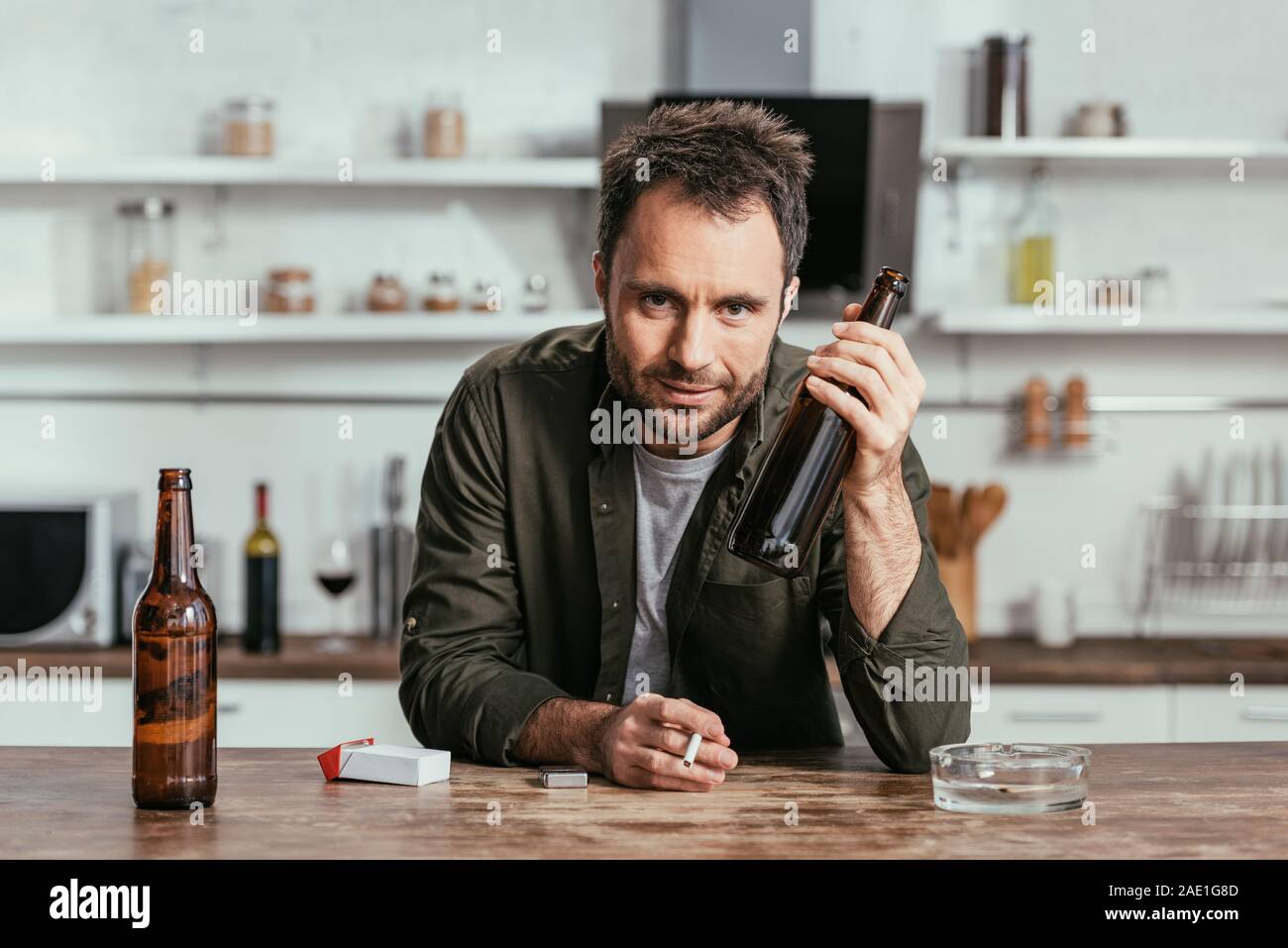 Alcohol addicted man with cigarette holding beer bottle and looking at ...