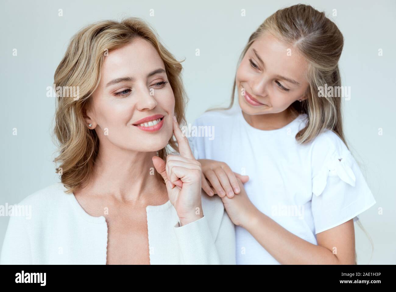smiling mother pointing with finger at cheek and daughter looking at ...