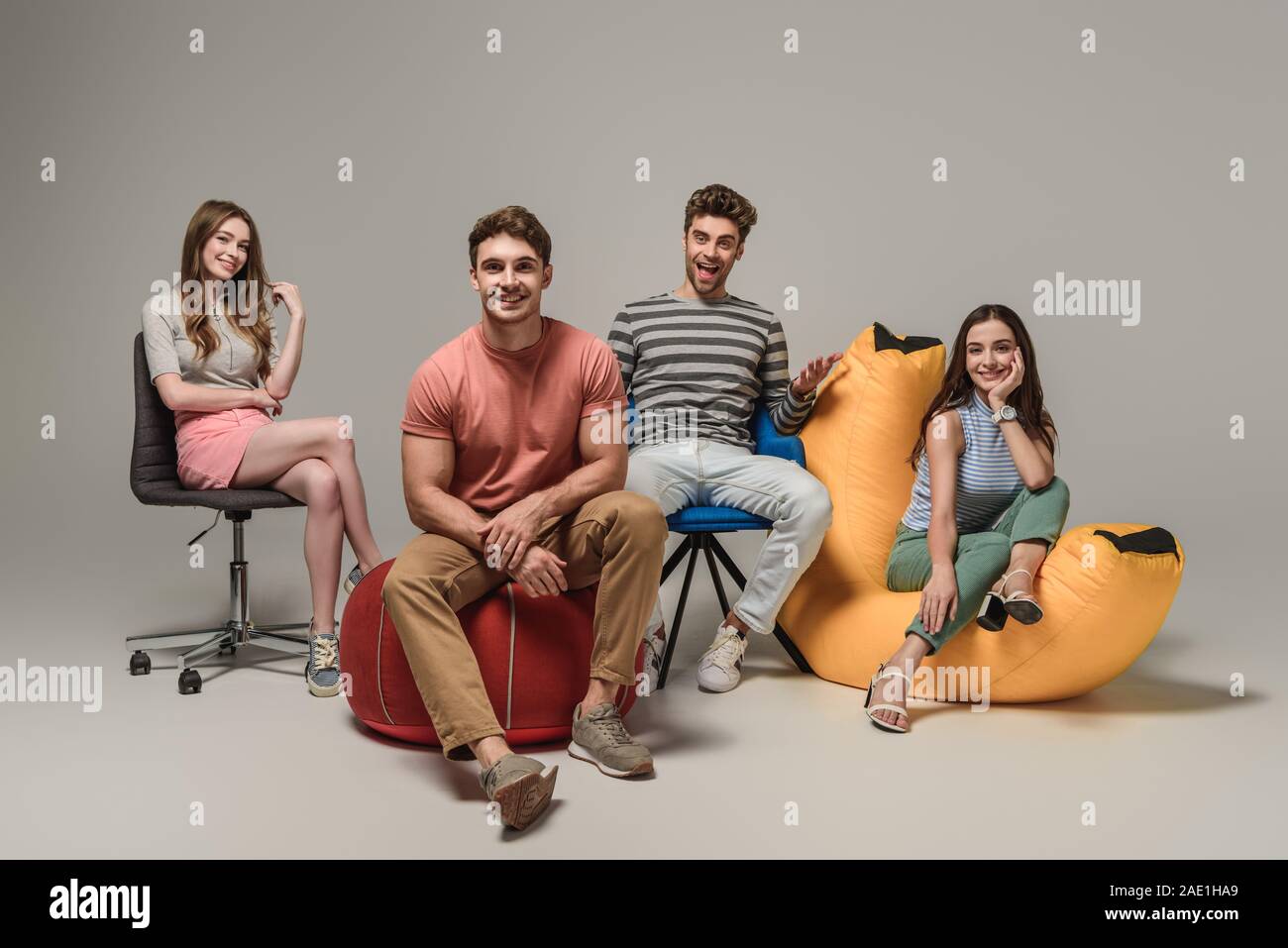 happy friends sitting on different chairs, on grey Stock Photo - Alamy