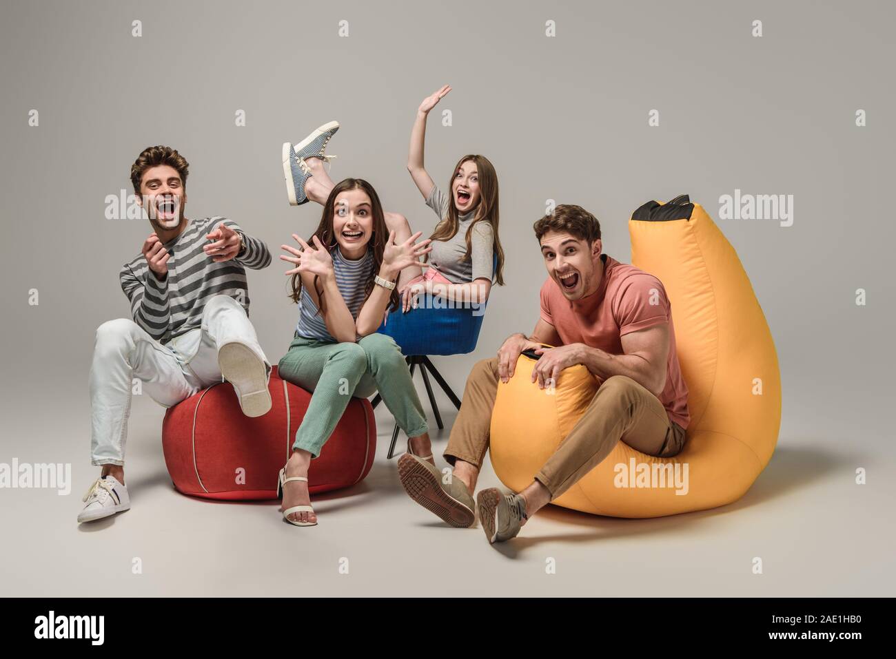funny laughing friends sitting on different chairs, on grey Stock Photo ...