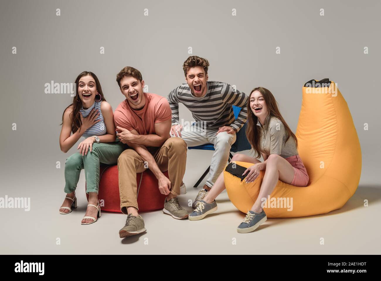 emotional friends laughing and sitting on different chairs, on grey ...