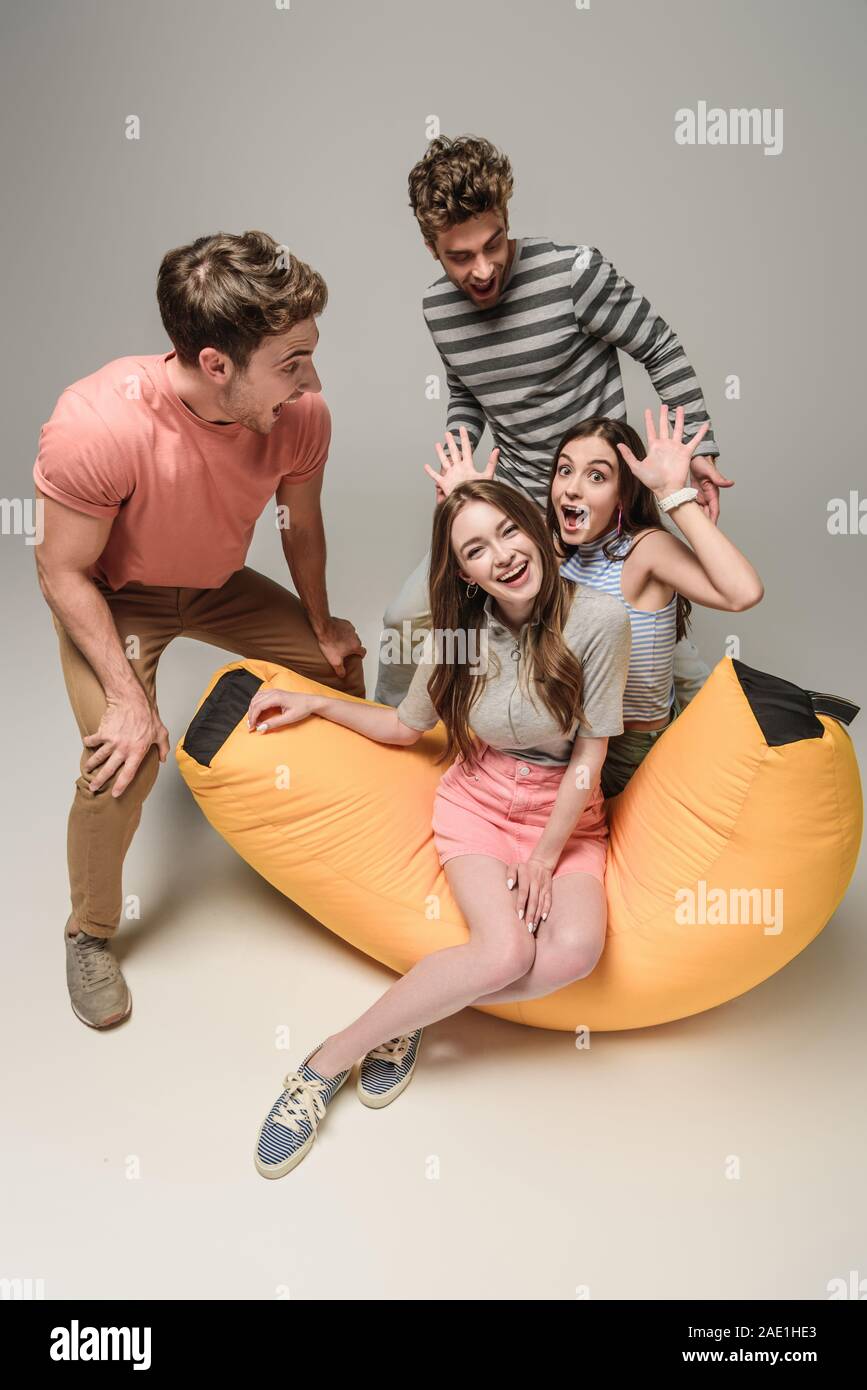 shocked friends sitting on bin bag chair together, on grey Stock Photo ...