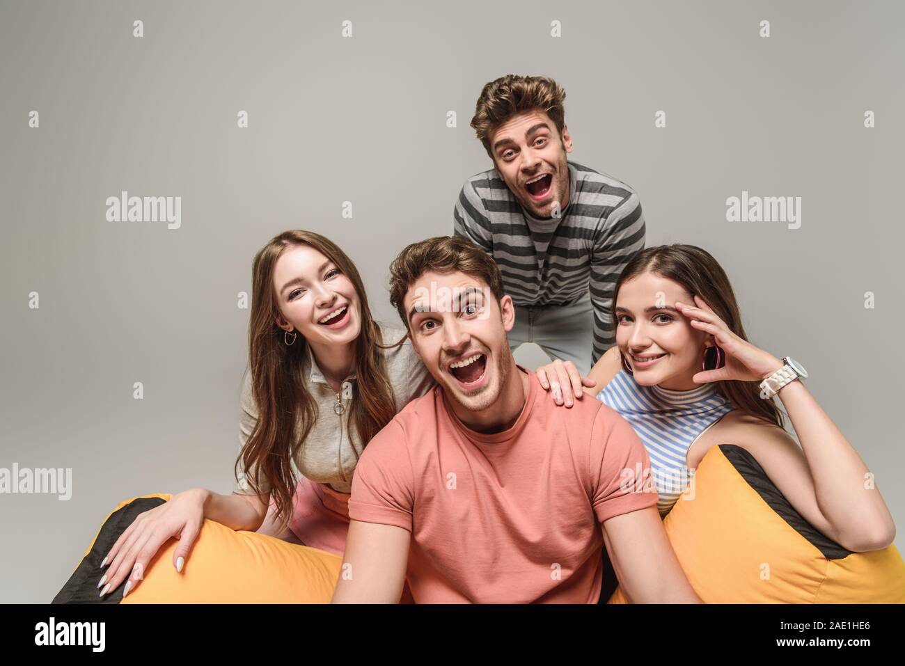 excited friends sitting on bin bag chair together, isolated on grey ...