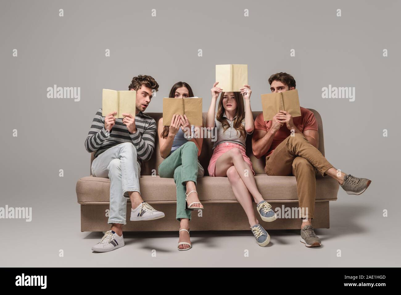 shocked friends reading books while sitting on sofa on grey Stock Photo ...