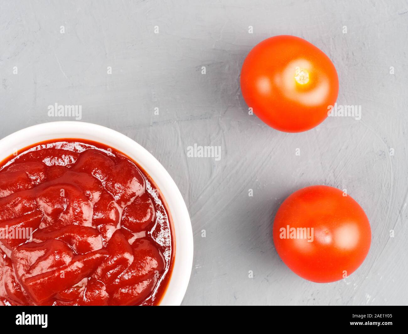 Tomato paste in a white bowl and tomatoes on a gray concrete background ...