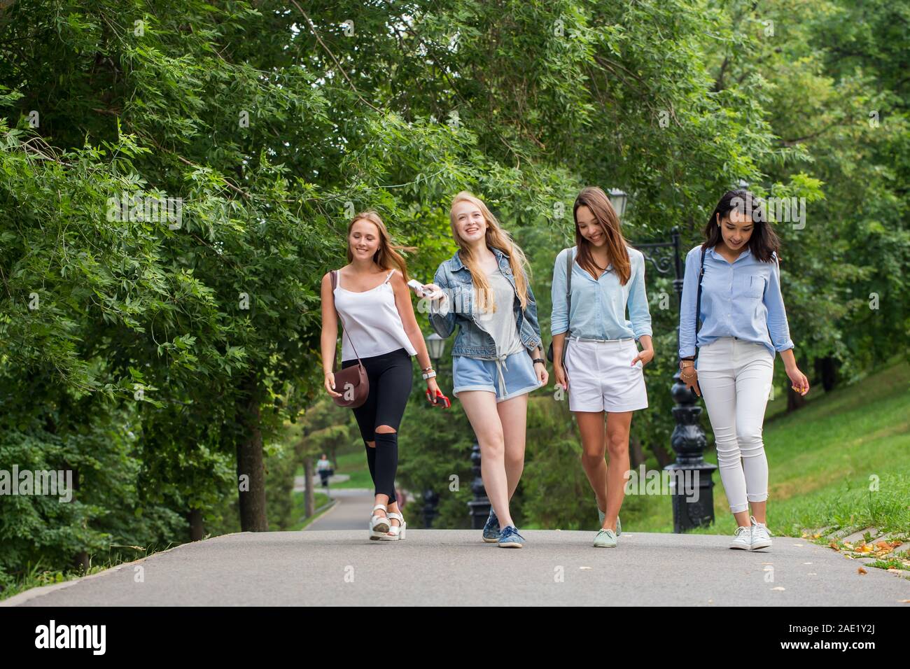 Four attractive young friends women talking and walking together on ...