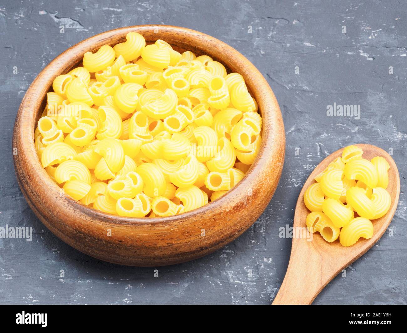Pasta helices type in wooden bowl and spoon on a black concrete ...