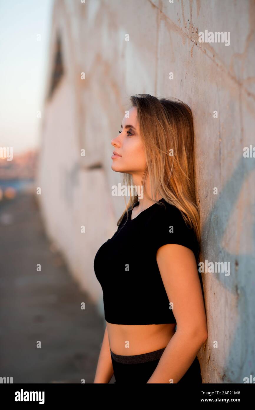 Sideways portrait of beautiful blonde woman in black top near wall of ...