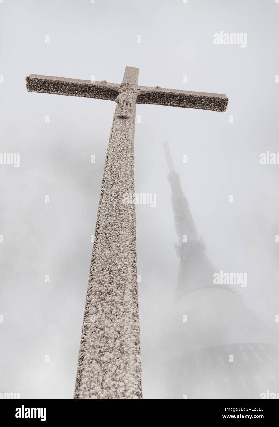 Snow covered Jesus Christ crucifix. Artistic wintry scene with transmitter station in fog ...