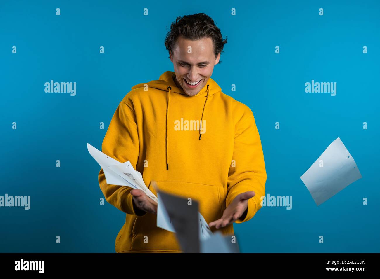 Young man throwing papers documents into air and smiling on blue ...